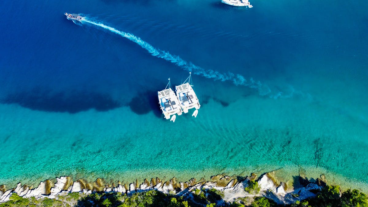 Aerial view of catamarans moored near a rocky coast in turquoise waters