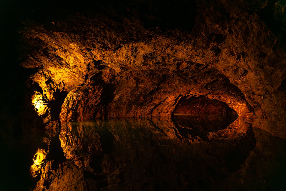 Dimly lit cave interior with stalactites reflected in still underground water