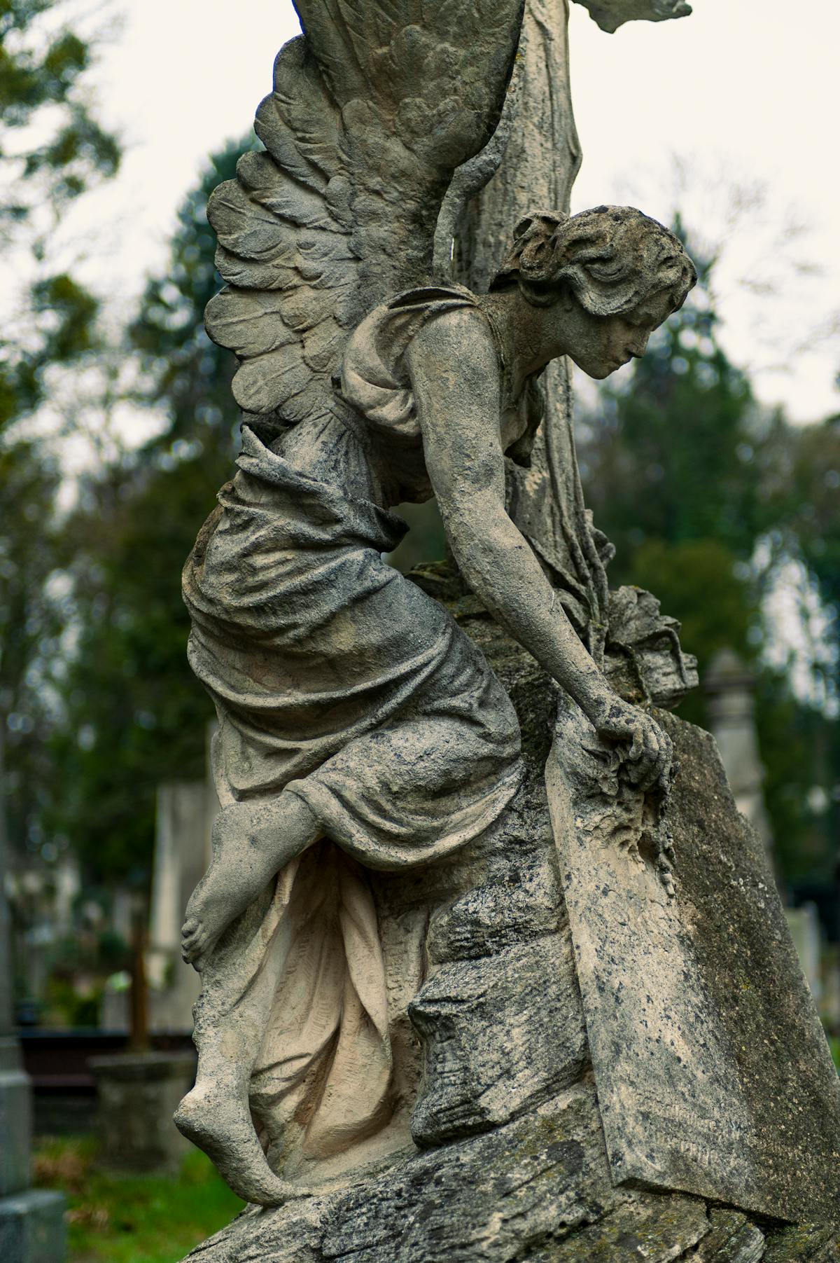 Detailed stone angel sculpture standing among old graves in a serene cemetery
