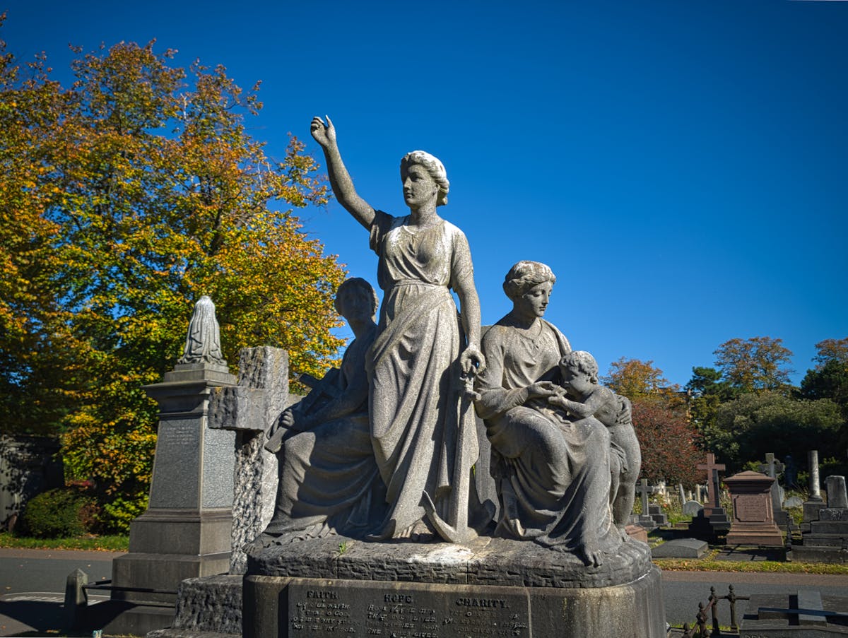 Row of stone statues and monuments in a cemetery with autumn colored trees