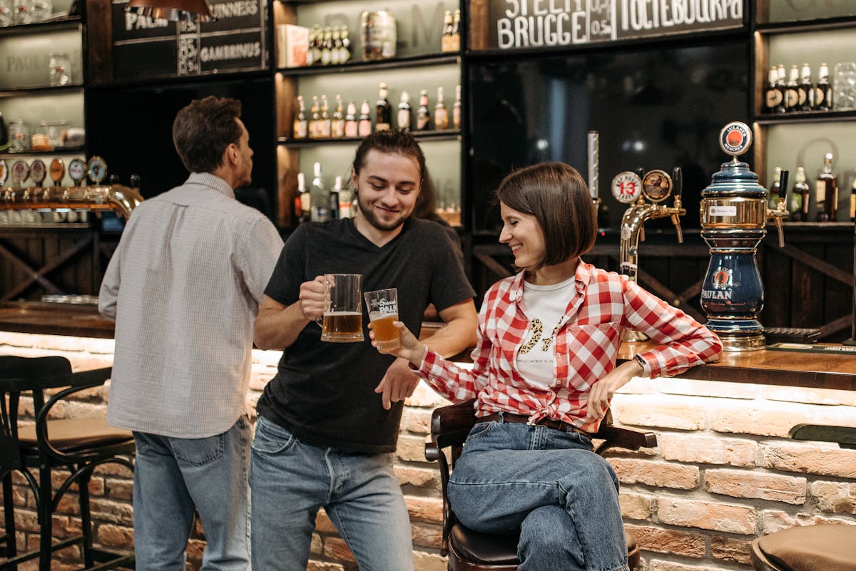 Young adults clinking beer mugs together at a lively indoor bar