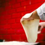 Chef skillfully stretches pizza dough in a Naples pizzeria with red brick walls
