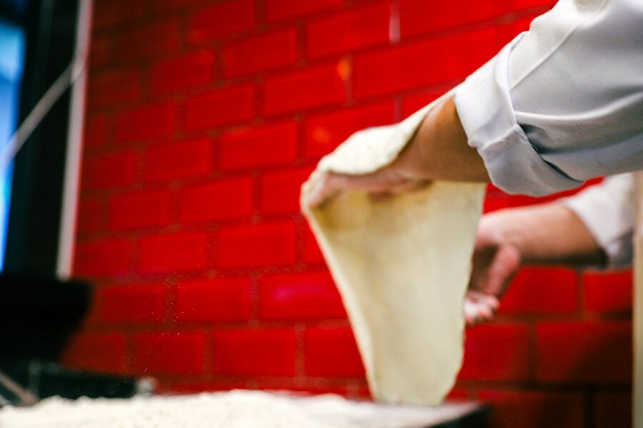 Chef skillfully stretches pizza dough in a Naples pizzeria with red brick walls