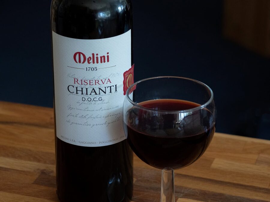 Bottle of Melini Chianti Riserva DOCG with a glass of red wine on wooden surface