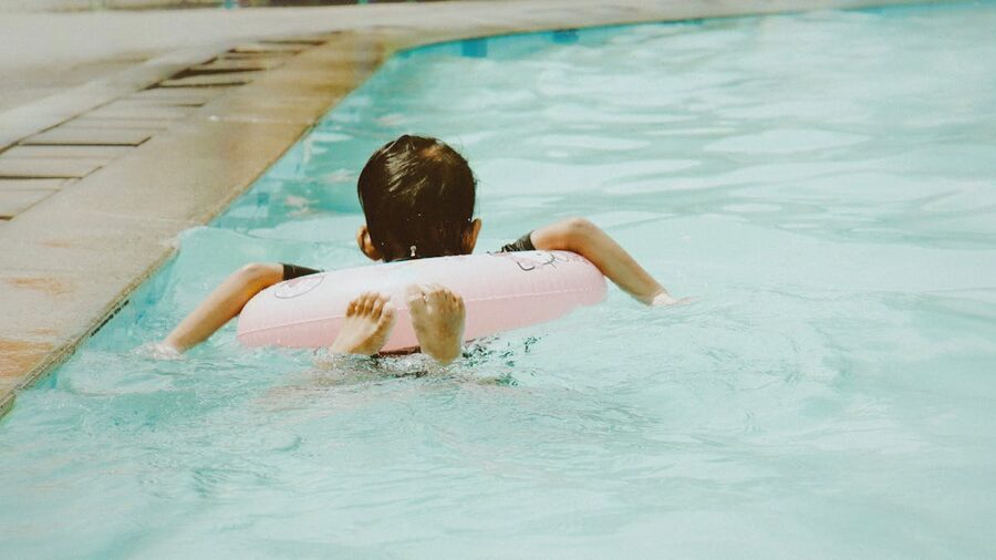 A young child swimming in a pool using a pink float on a sunny day