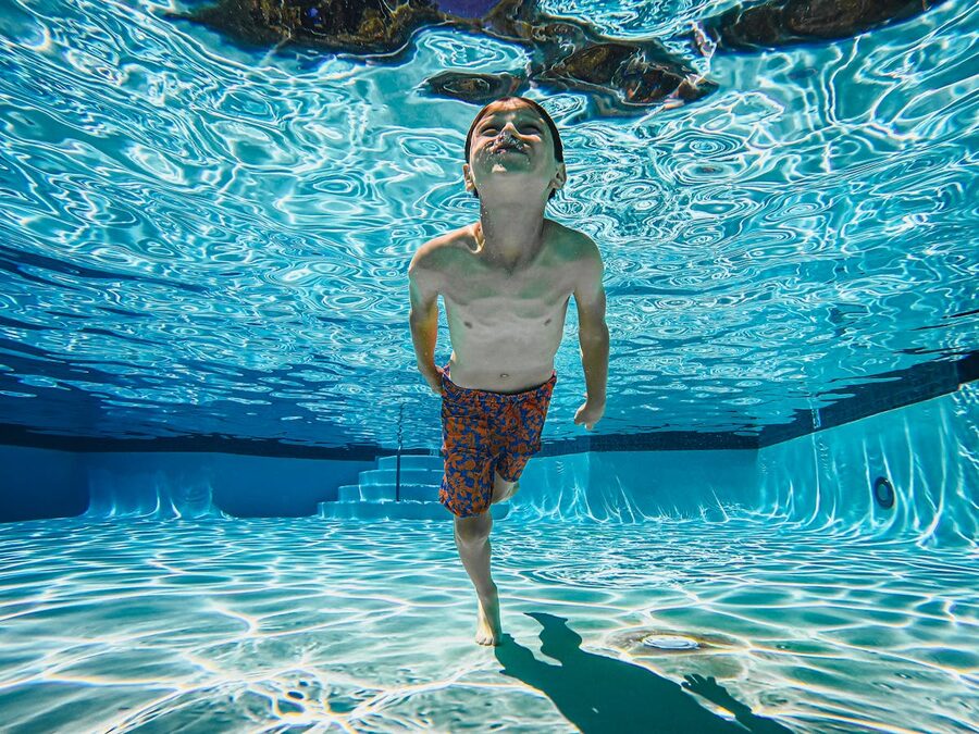 A child swimming underwater in a bright blue pool on a sunny day