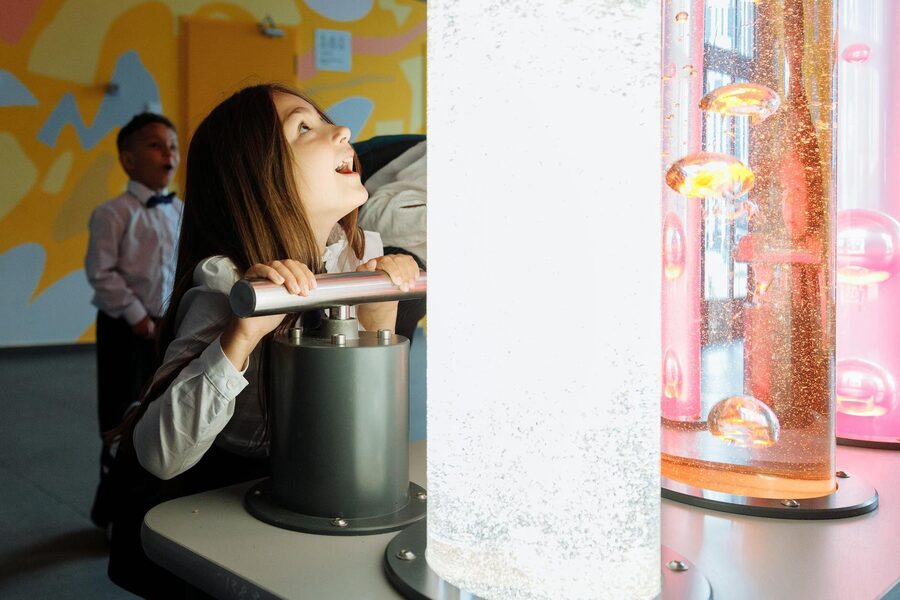 Children interacting with a colorful science exhibit featuring vibrant liquids and lights