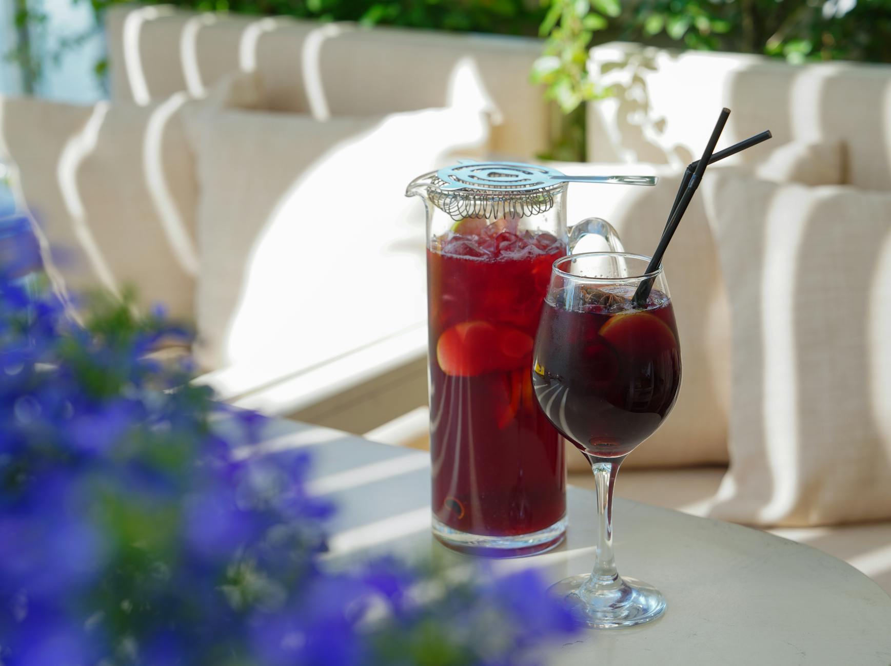 Sangria in a glass and pitcher with straws on a sunny outdoor table