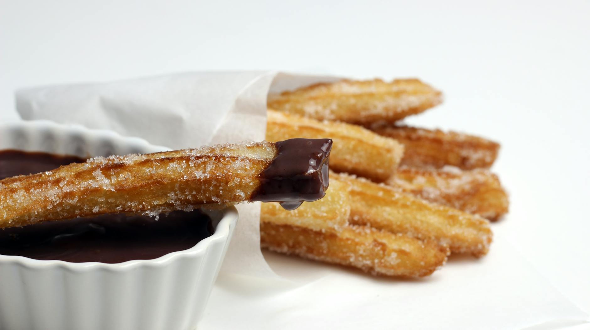 Churros coated in sugar being dipped in chocolate sauce