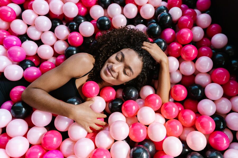 Joyful woman relaxing in a colorful ball pit filled with pink and black plastic balls