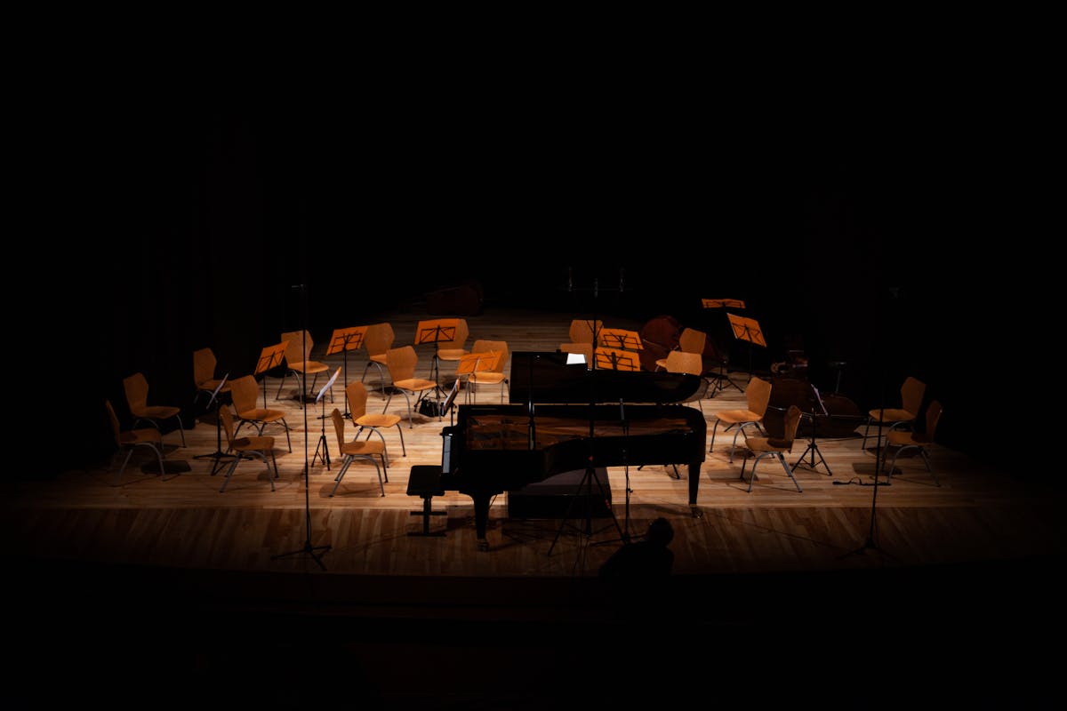 Empty concert hall stage with a grand piano and chairs