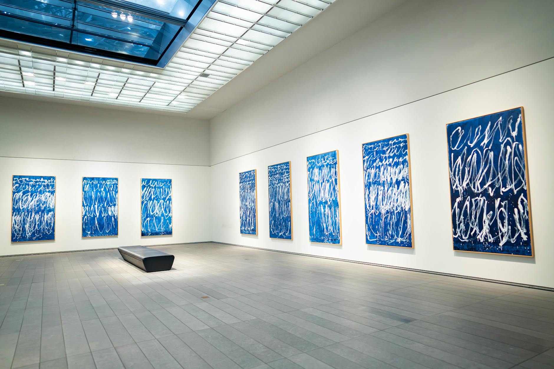 Spacious modern art gallery featuring a collection of blue abstract paintings on white walls