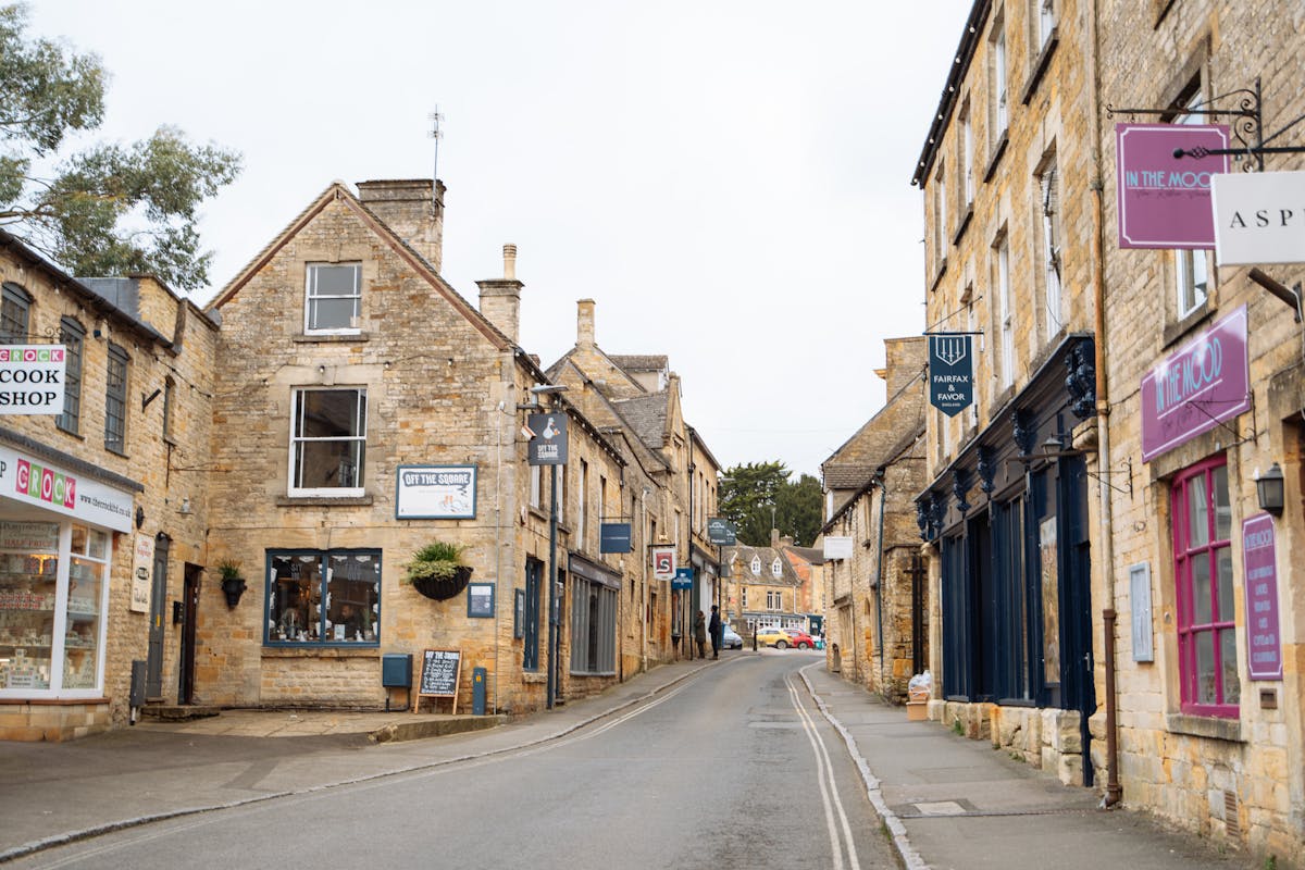 Narrow stone-walled lane through a Cotswolds village with flowers and green hedges