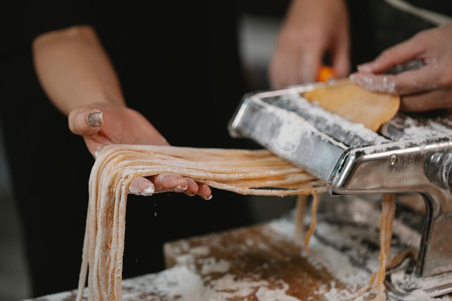 A couple making fresh pasta noodles with a pasta cutter on a floured table