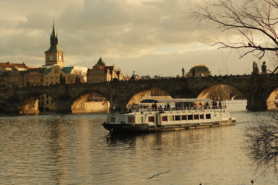 Cruise boat sailing under Charles Bridge on the Vltava River in Prague during golden hour