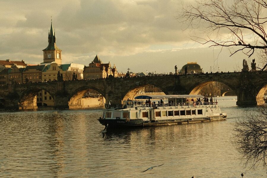 Cruise boat sailing under Charles Bridge on the Vltava River in Prague during golden hour