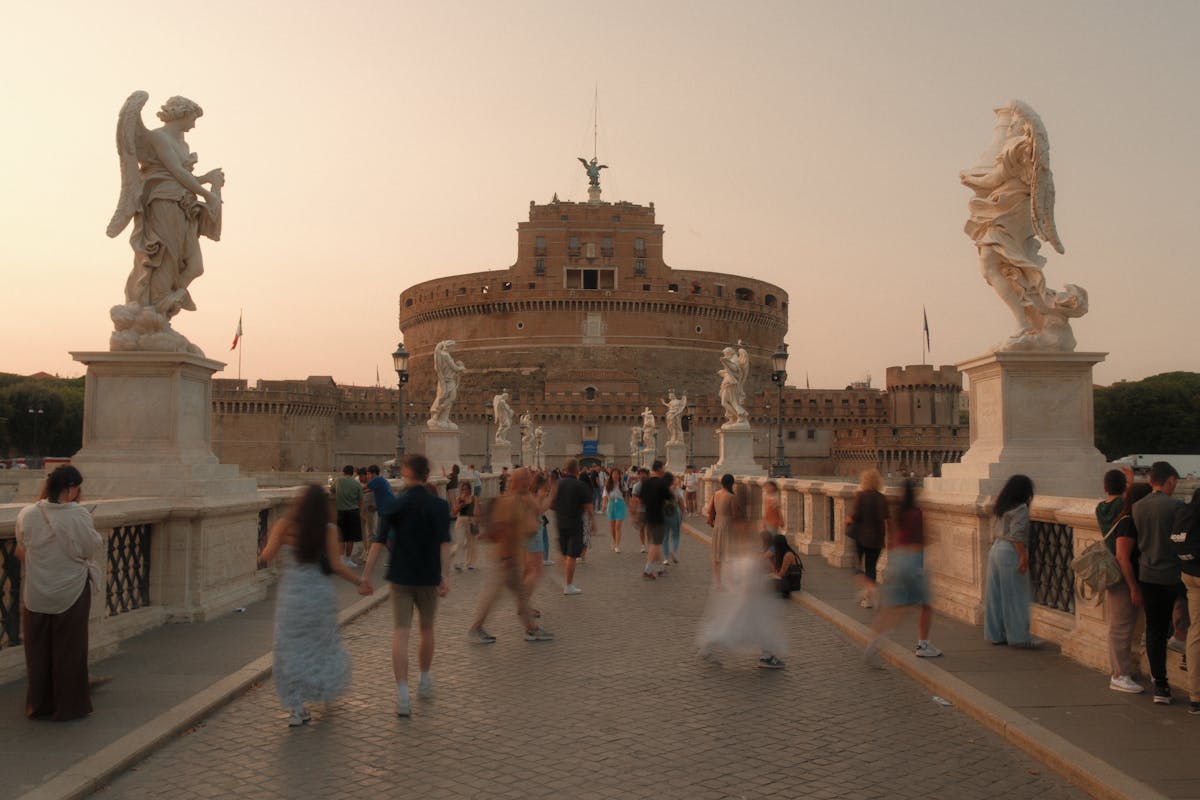 People walking across Ponte Sant Angelo bridge at sunset with Castel Sant Angelo in Rome