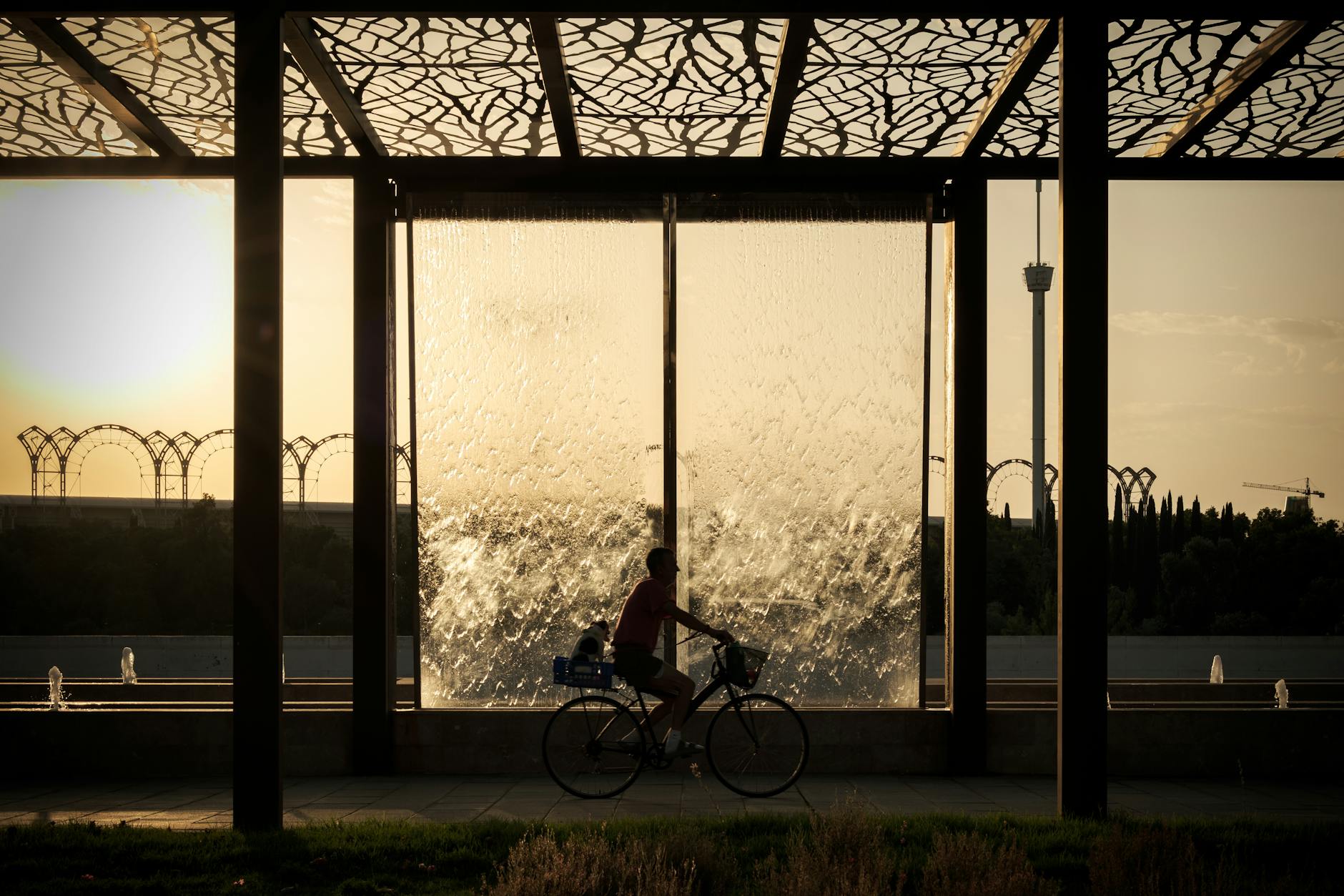 Cyclist riding past a modern waterfall structure at sunset in Seville