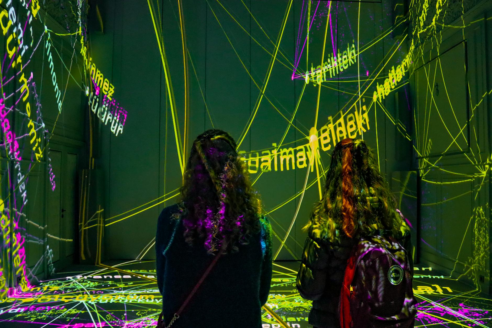 Two women observing a dynamic text projection art installation in a dark room