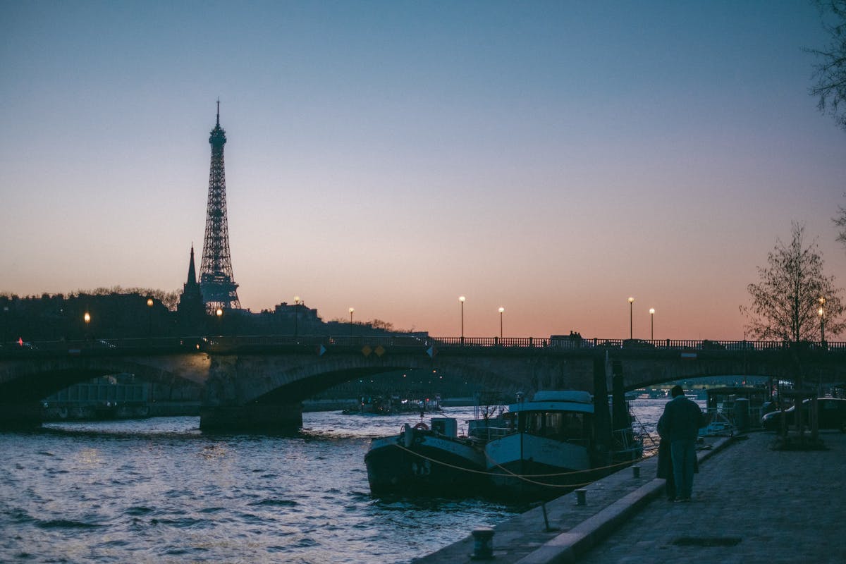The Eiffel Tower against a sunset sky seen from the Seine River bank