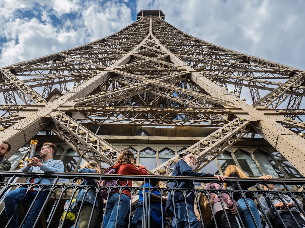 Visitors on the Eiffel Tower viewing deck looking up at the iron lattice structure
