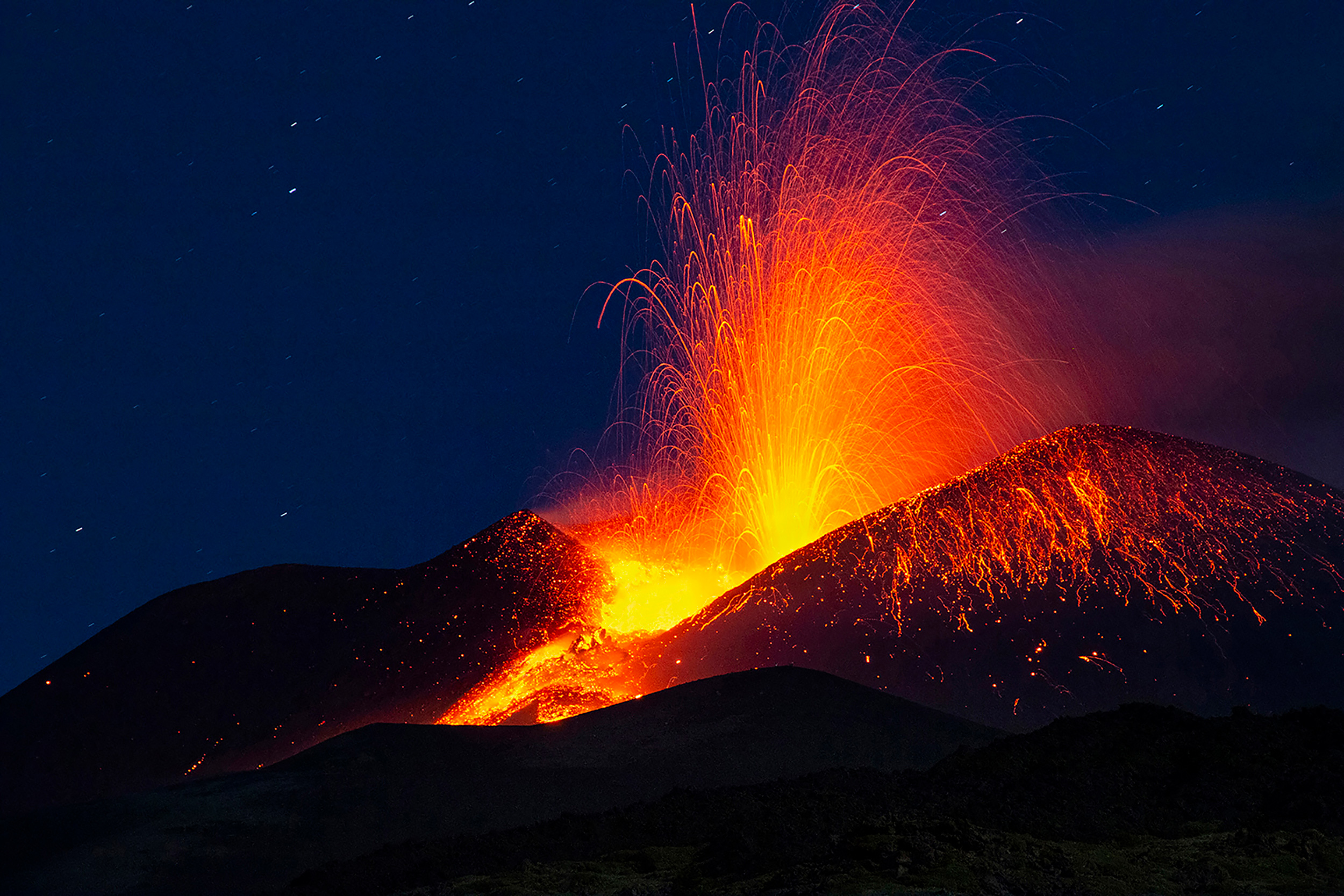 Nighttime eruption of Mount Etna in 2021 with orange lava illuminating the sky