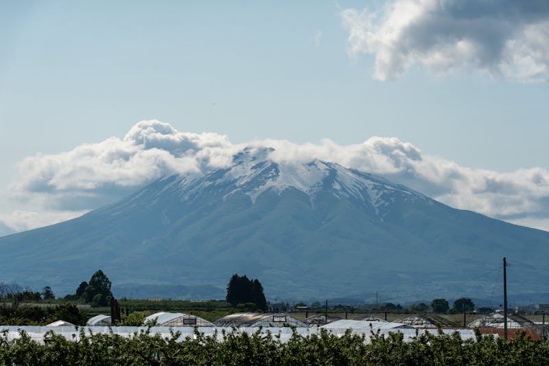 Mount Etna volcano with cloud cover and green landscape in foreground