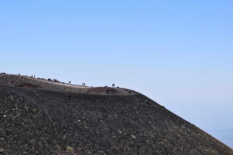 People hiking on the volcanic terrain at the top of Mount Etna in Sicily