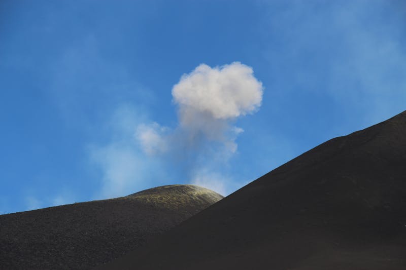 Mount Etna volcanic hills with smoke rising from the crater under blue sky
