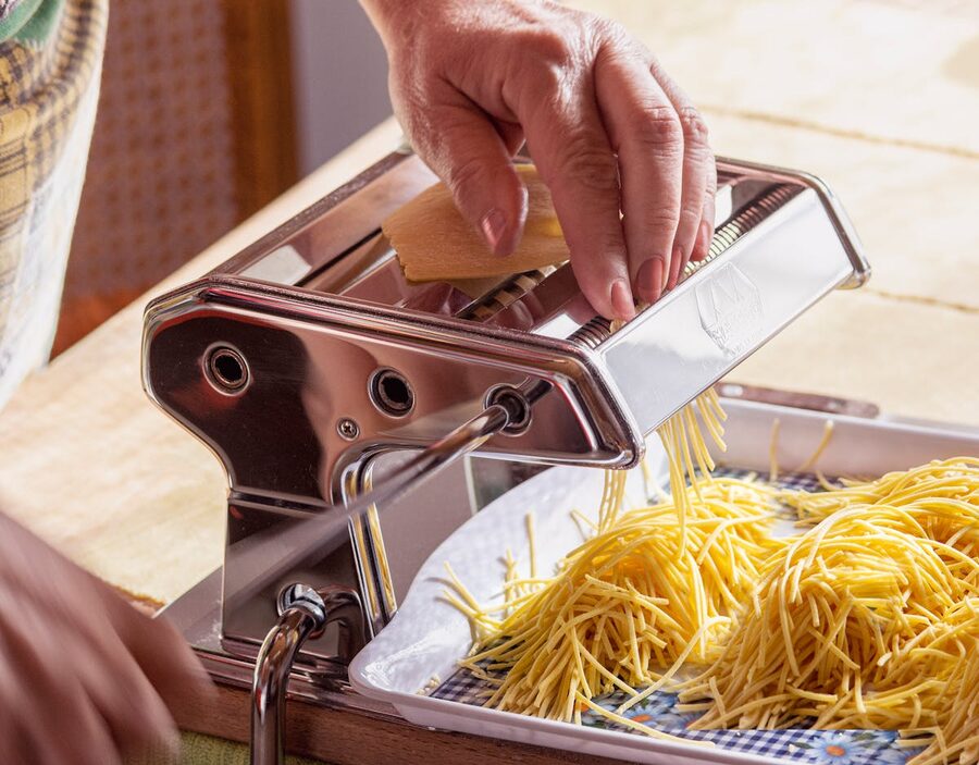 Senior adult making fresh pasta using a pasta maker in a kitchen