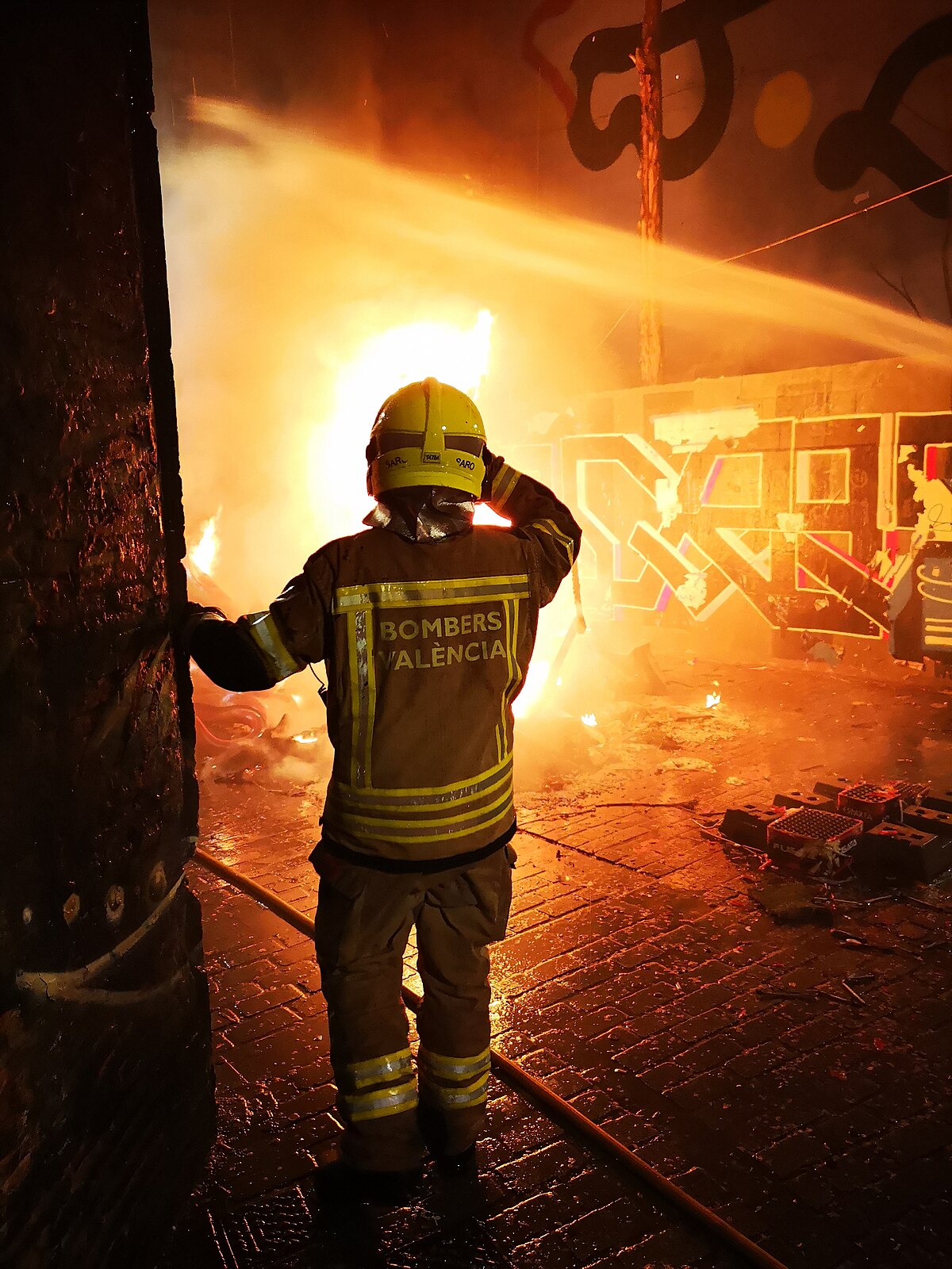 A falla monument engulfed in flames while a firefighter sprays water during La Crema in Valencia