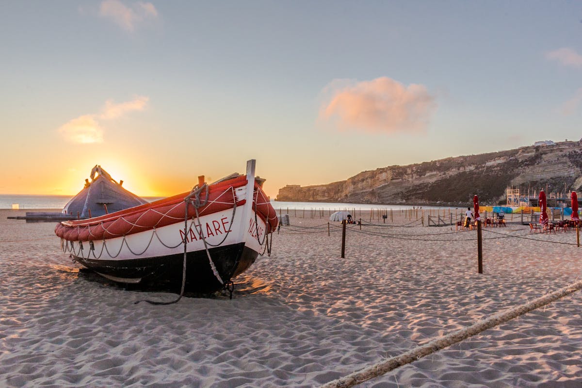 Traditional red and white fishing boat on the sandy beach at Nazaré Portugal at sunset
