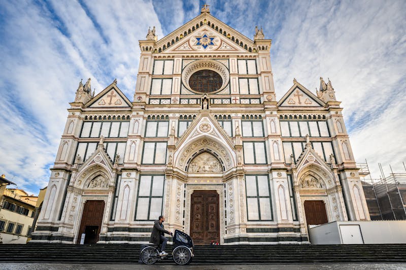 Cyclist passing the front of Basilica di Santa Croce in Florence Italy