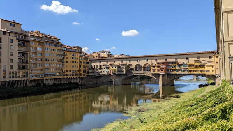 View of Ponte Vecchio and reflections on the Arno River in Florence on a sunny day