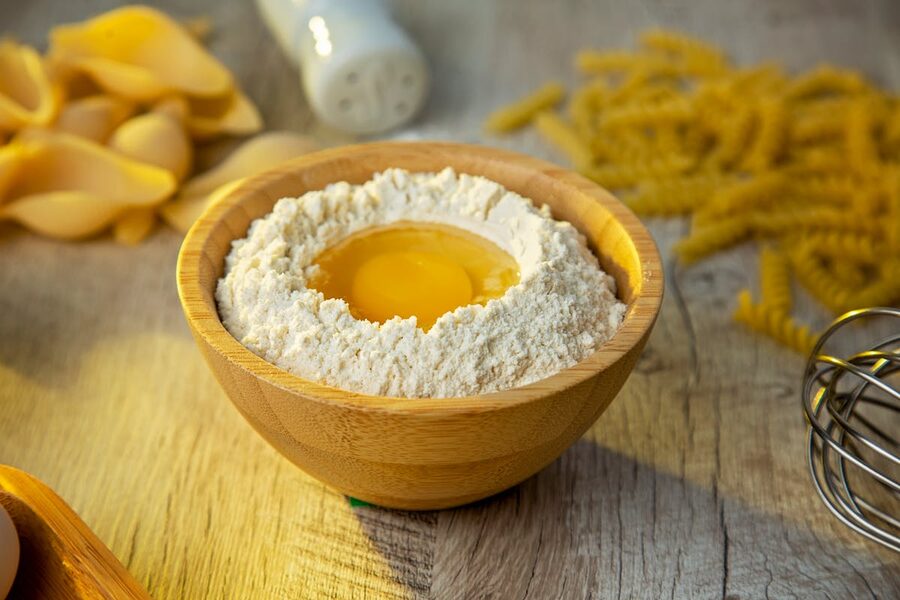 A wooden bowl with flour and egg yolk staged for making homemade pasta