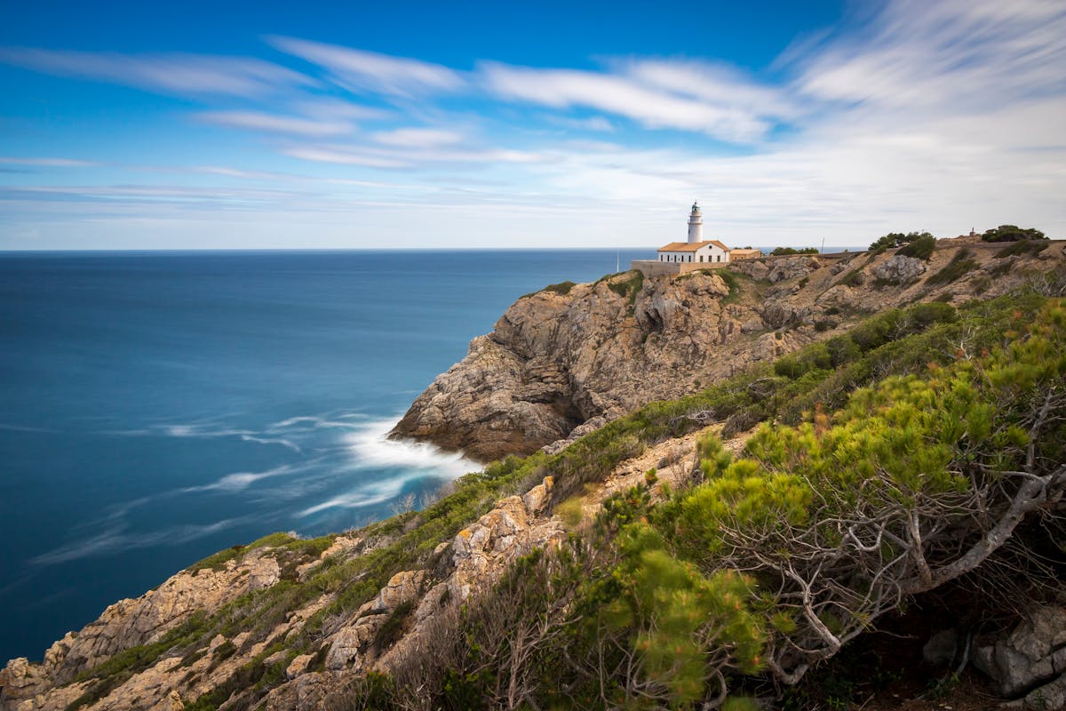 Lighthouse perched on rocky cliffs overlooking the Mediterranean Sea under clear blue sky