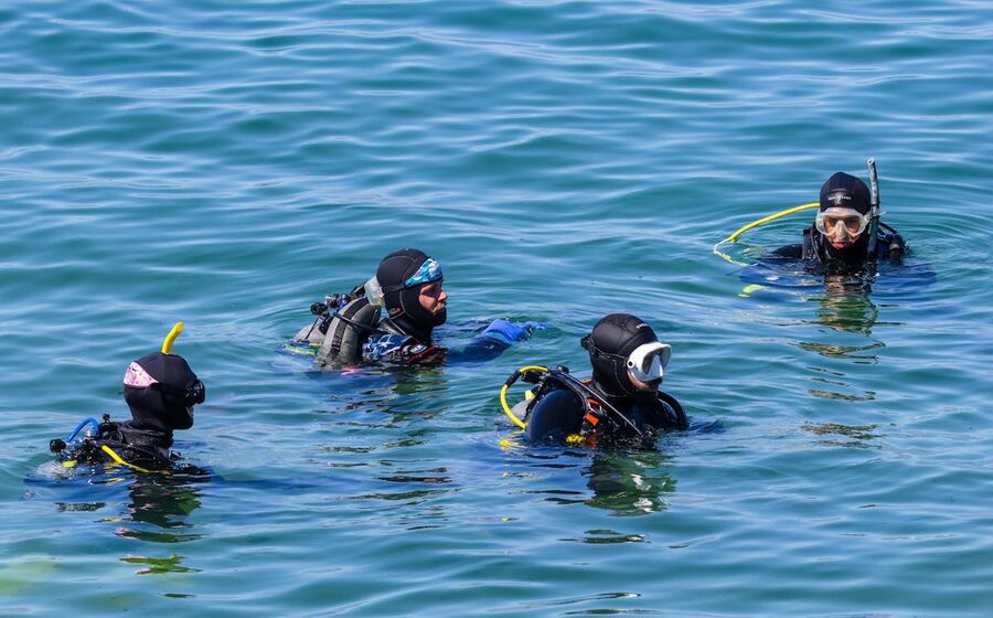Four scuba divers in wetsuits on the ocean surface preparing for a dive