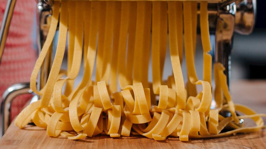Close-up of fresh pasta strands being made with a pasta machine in a kitchen