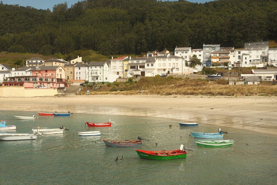 Charming coastal village in Galicia with boats and lush forest backdrop