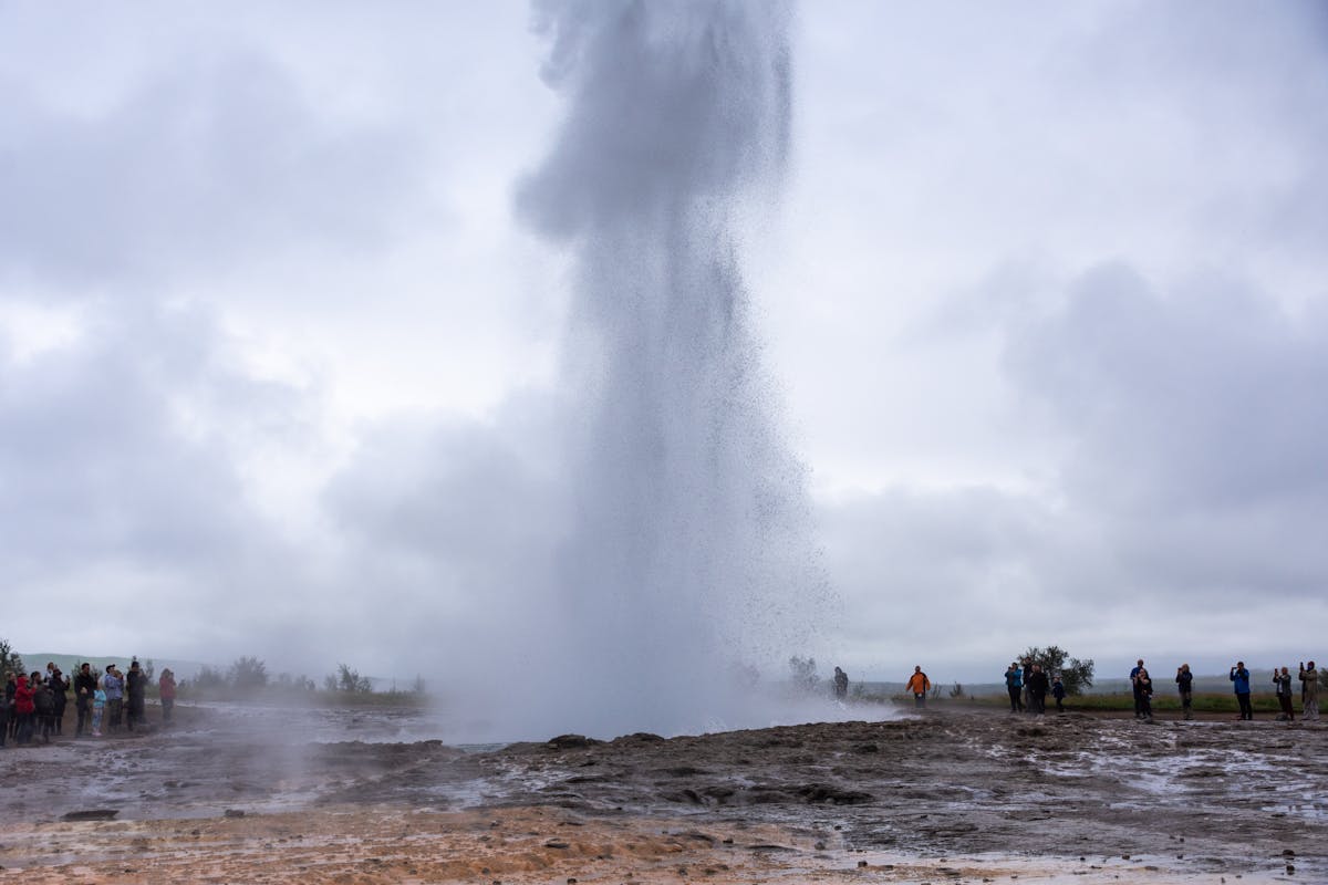 Geyser erupting in the Geysir hot spring area in Iceland under a cloudy sky