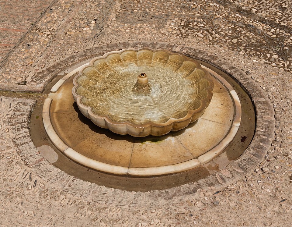 Stone fountain with flowing water surrounded by greenery in the Generalife gardens