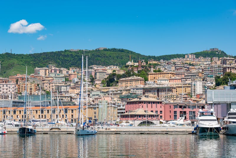 Sailboats moored in Genoa marina with colorful hillside buildings in the background