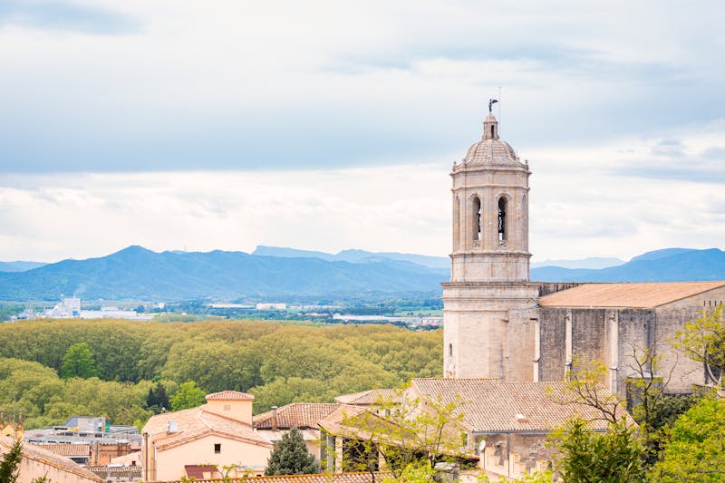 Stone bell tower of Girona cathedral with green hills and mountains in the background