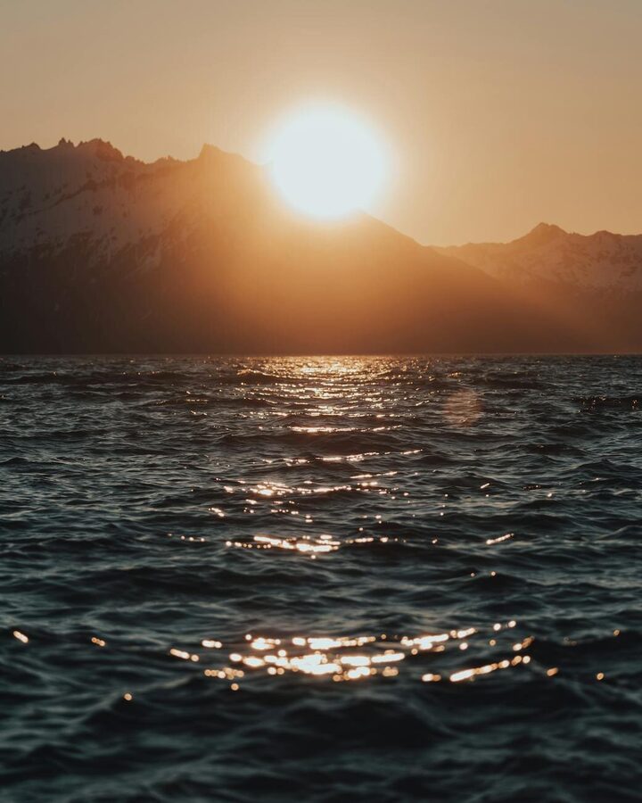 Lofoten mountains reflected in calm sea waters under golden sky