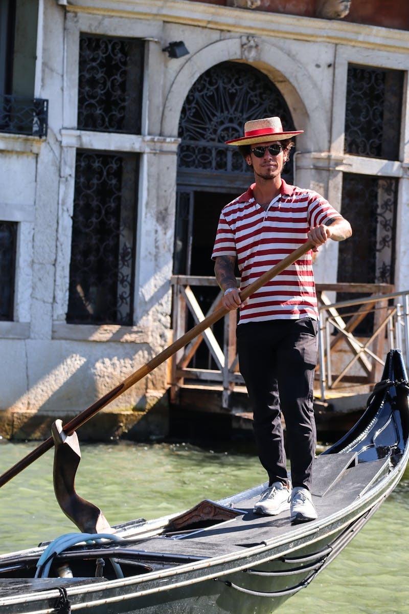 A gondolier in traditional attire rowing a gondola on a picturesque Venetian canal