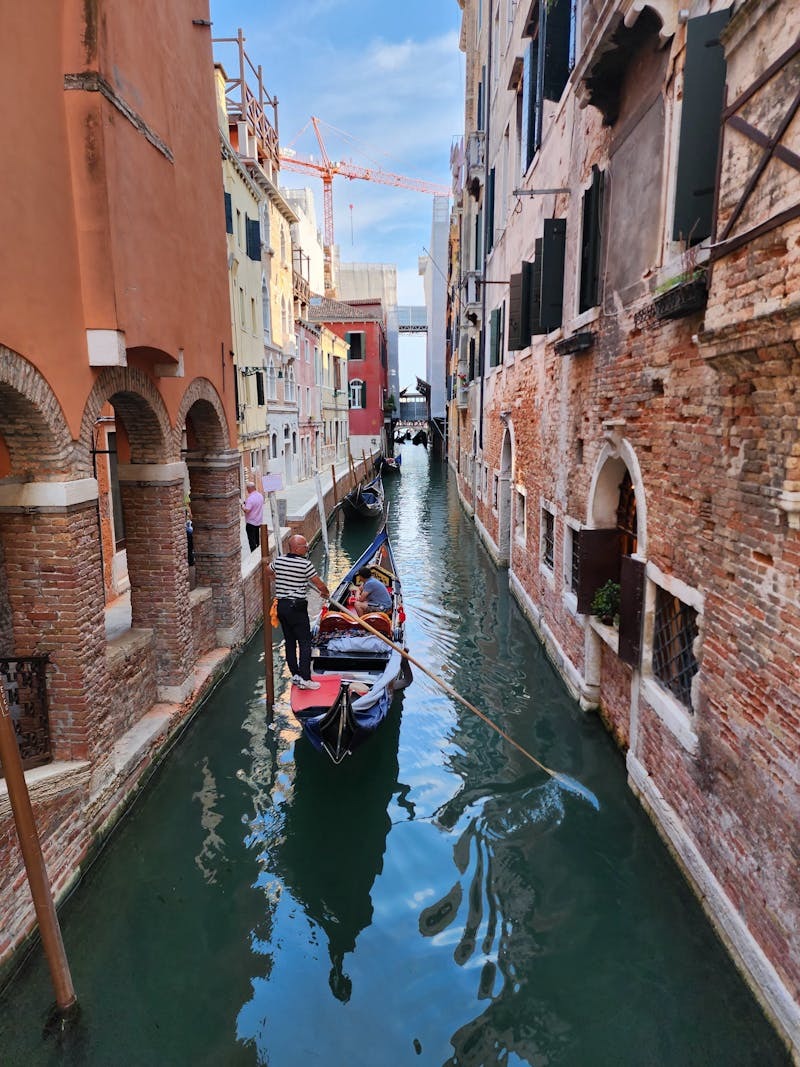A serene gondola ride navigating a narrow canal in Venice, Italy, under a clear sky