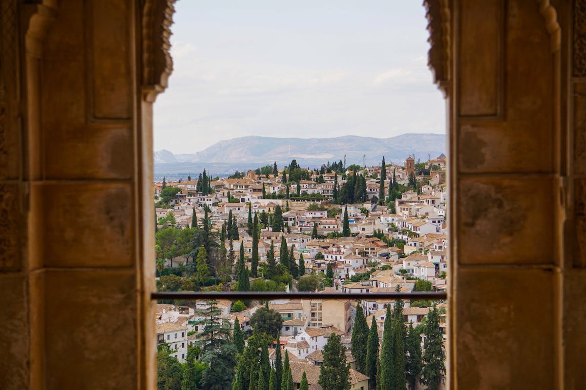 A view of the city of Granada and distant mountains framed through an ornate stone archway at the Alhambra