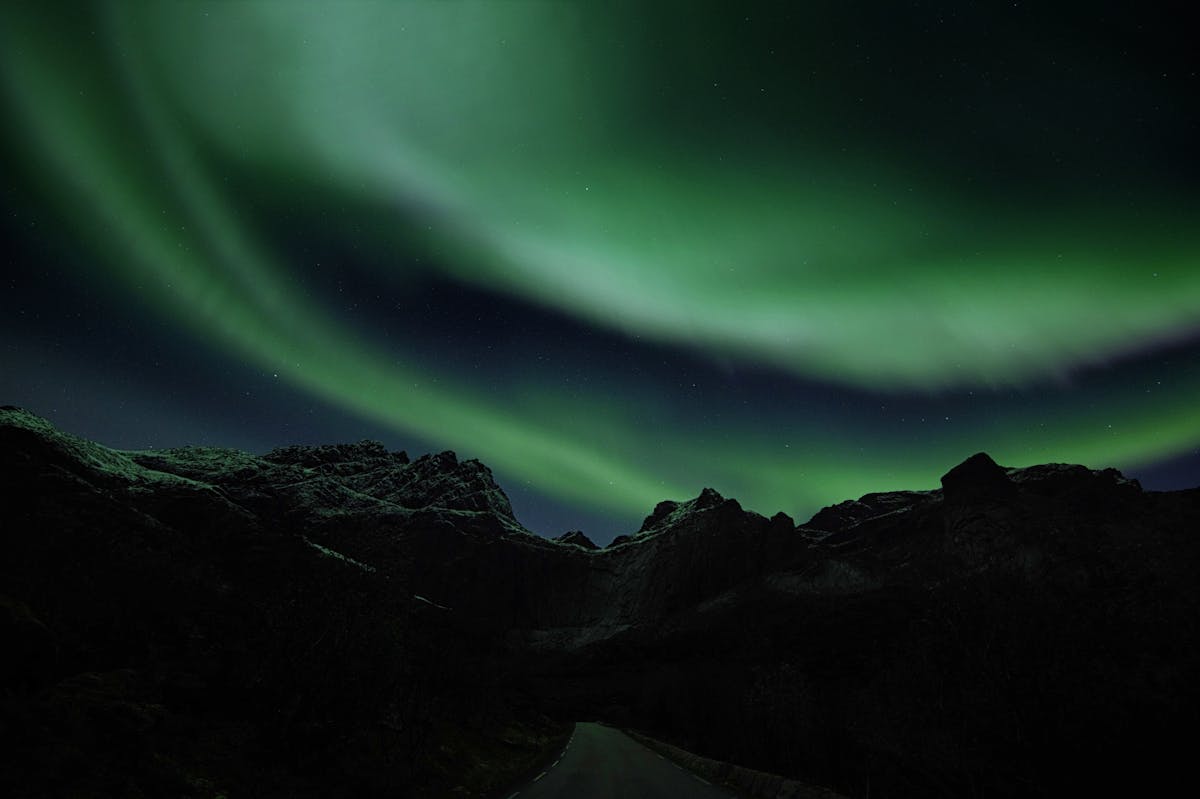 Green aurora borealis illuminating the night sky above rugged mountains in Norway