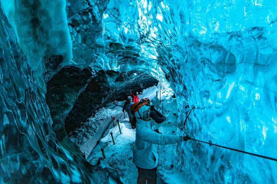 Group exploring a stunning blue ice cave, showcasing glacial textures and colors.