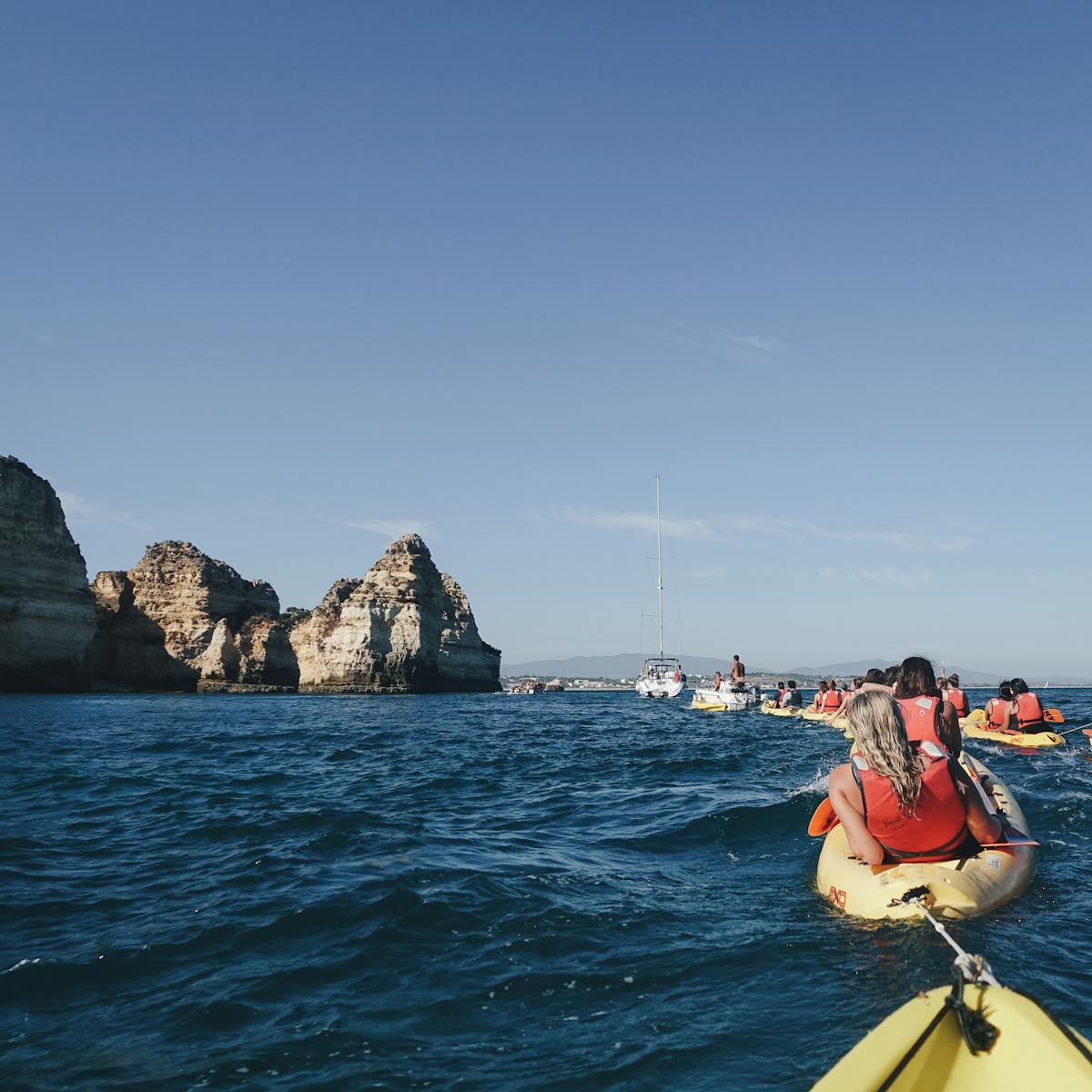 Group of kayakers paddling along ocean cliffs in clear blue water
